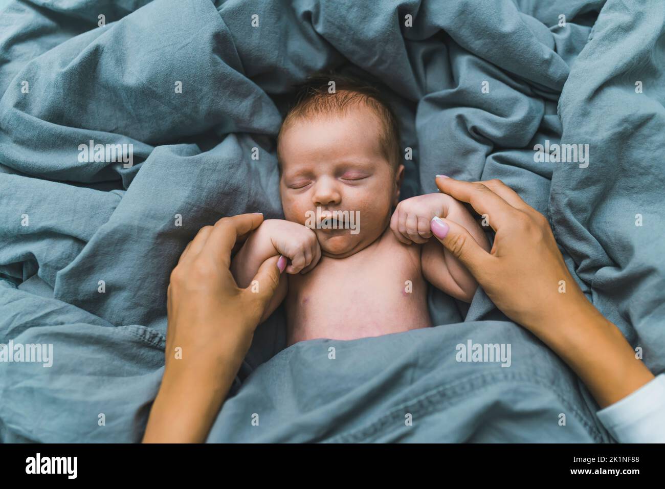 White baby boy sleeping in soft blue bed sheets and hands of his mom ...
