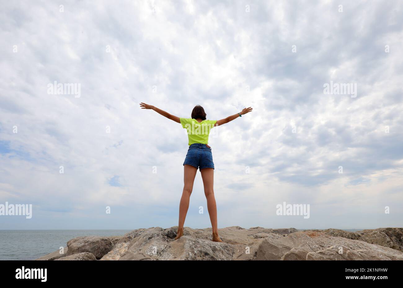 young girl performs gymnastic exercises on the rocks by the sea without ...