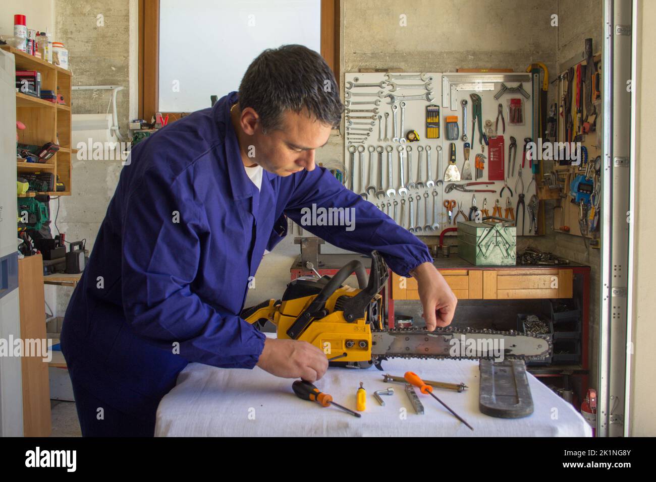 Image of a mechanic in his garage repairing a chainsaw by tensioning ...