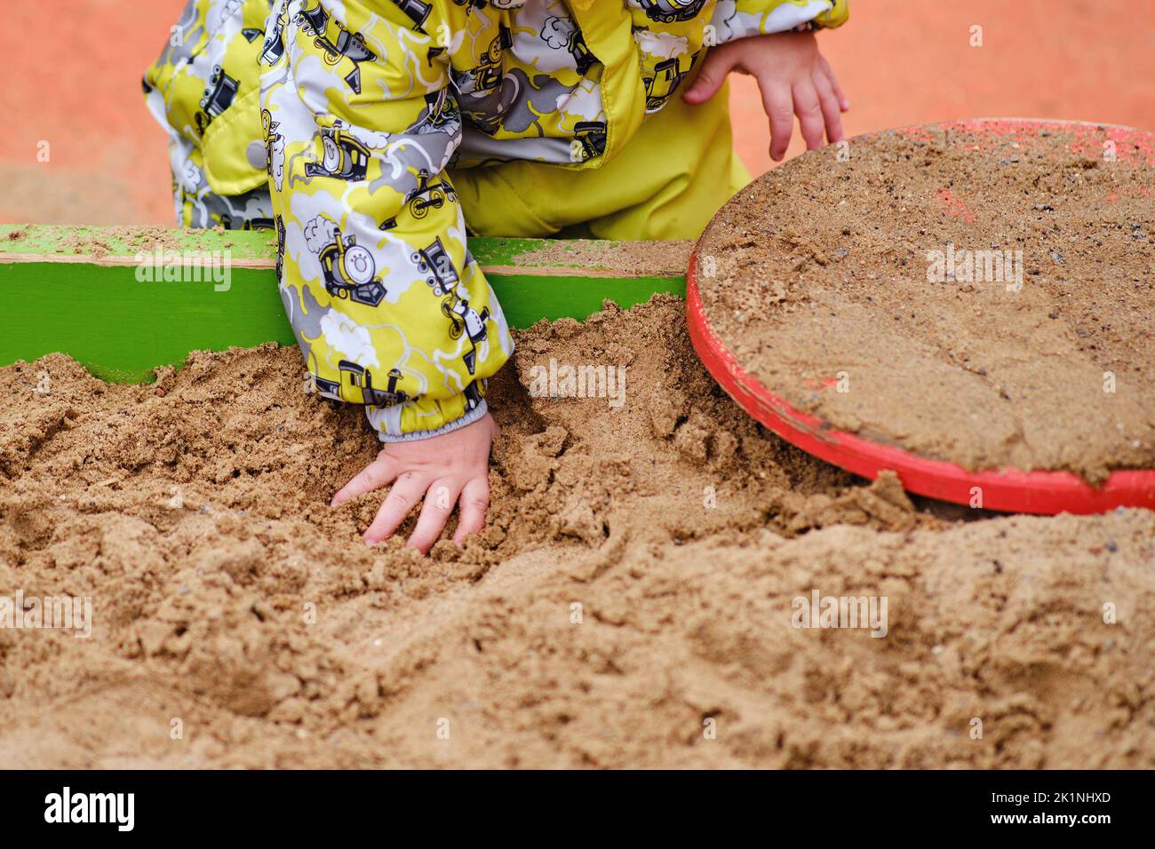 Happy toddler baby boy is playing in the sandbox. A child in warm ...