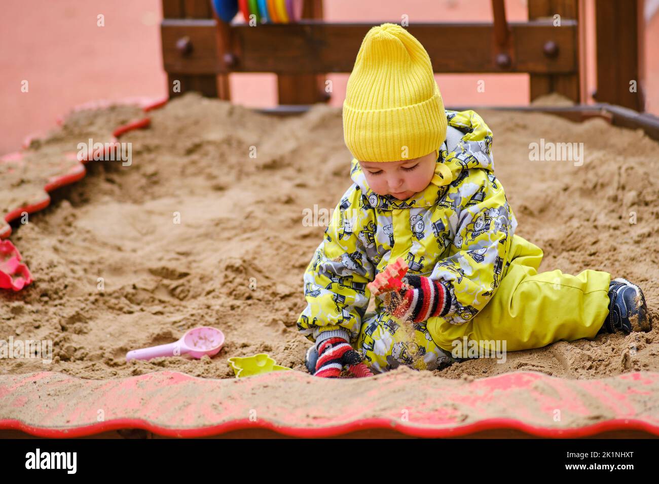 Happy toddler baby boy is playing in the sandbox. A child in warm ...