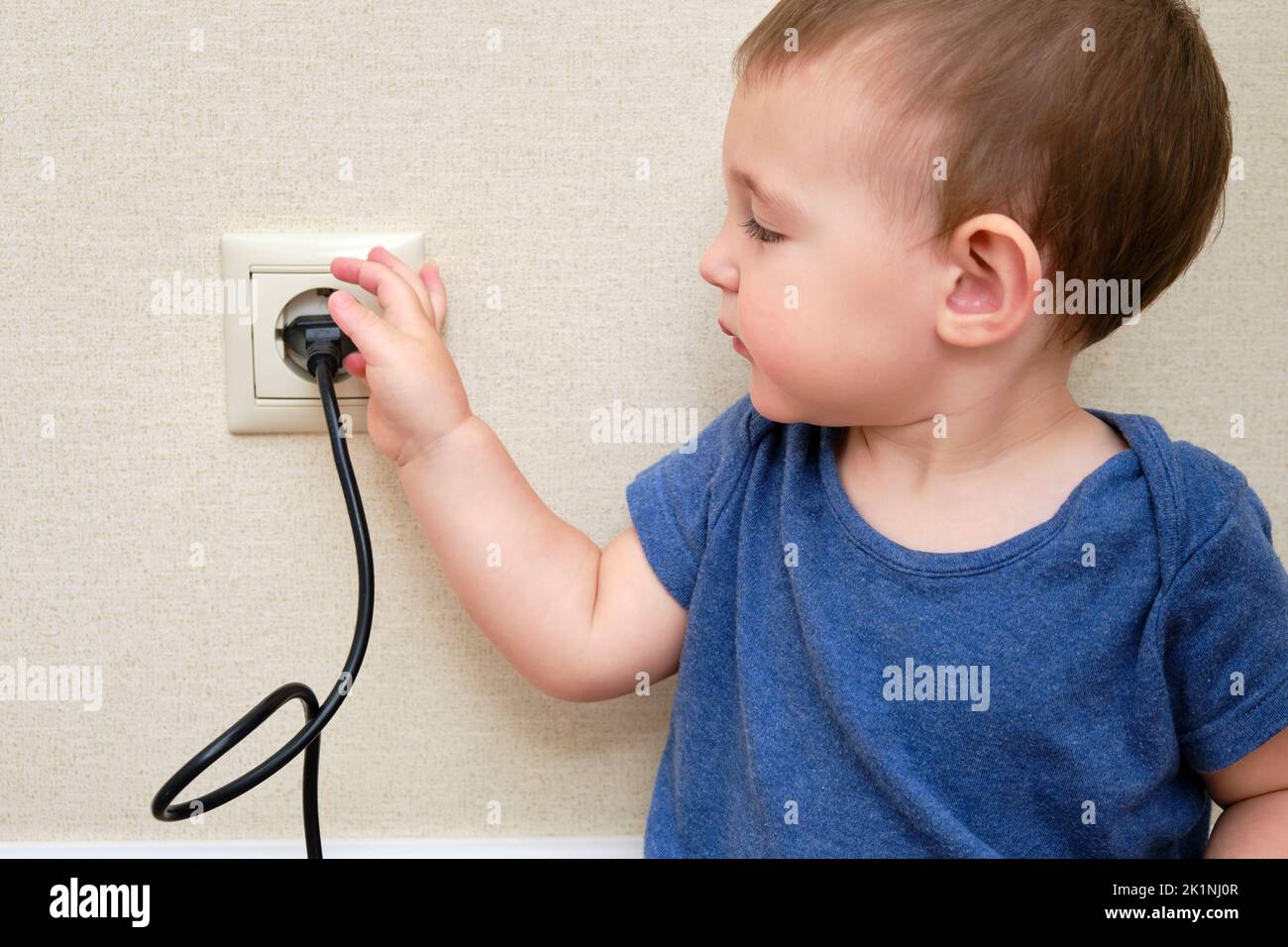 Toddler baby is playing with wire at the electrical outlet. Child boy ...