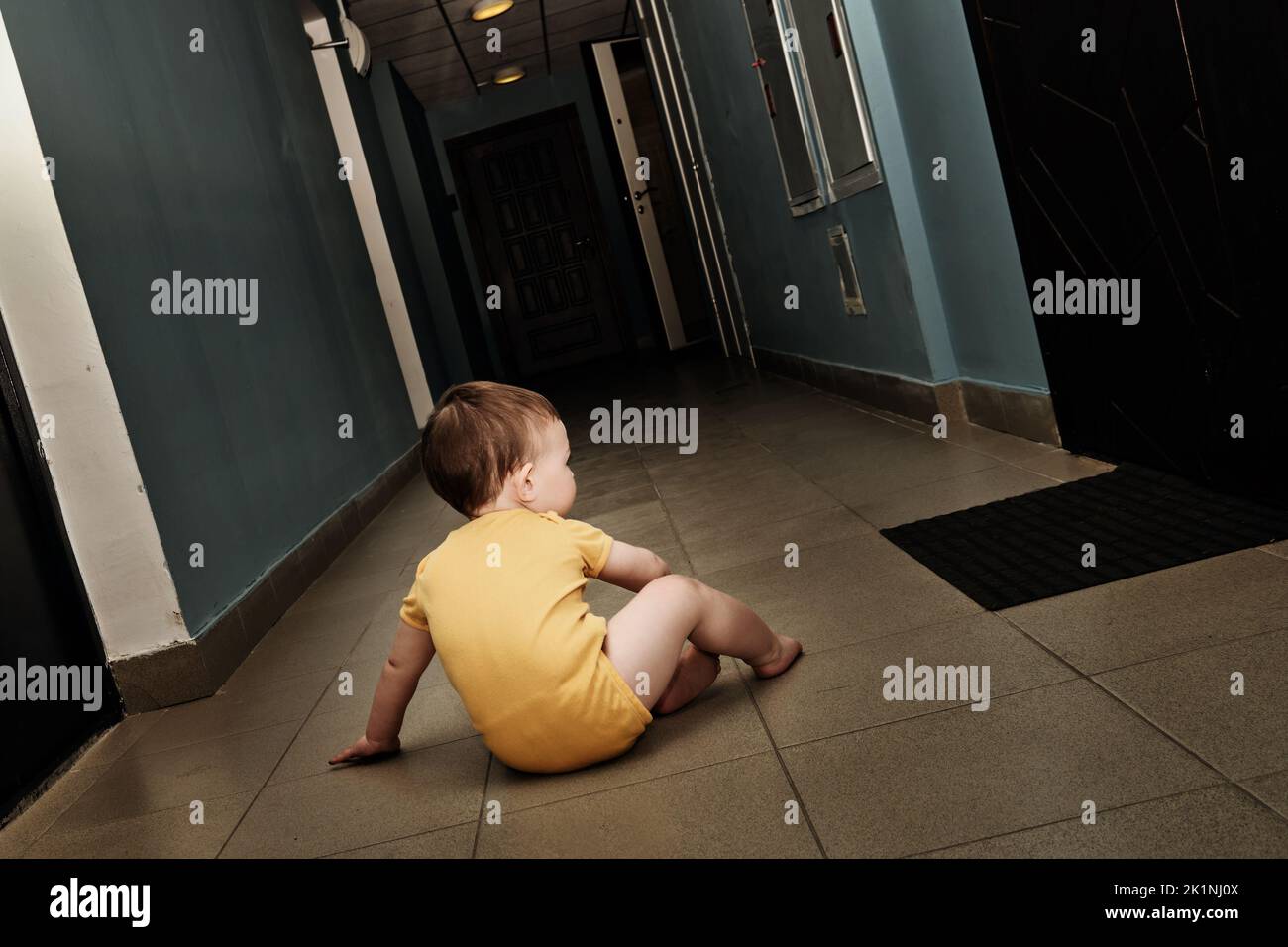 Toddler baby alone in a dark corridor. A lonely child boy sits in the ...