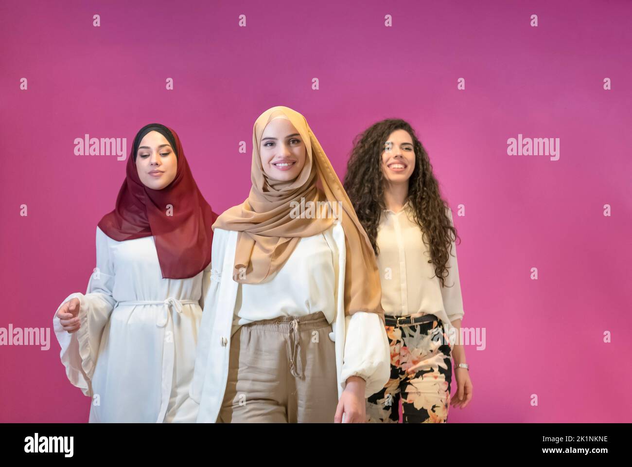 three Muslim women in hijab in a modern clothes pose against a pink ...