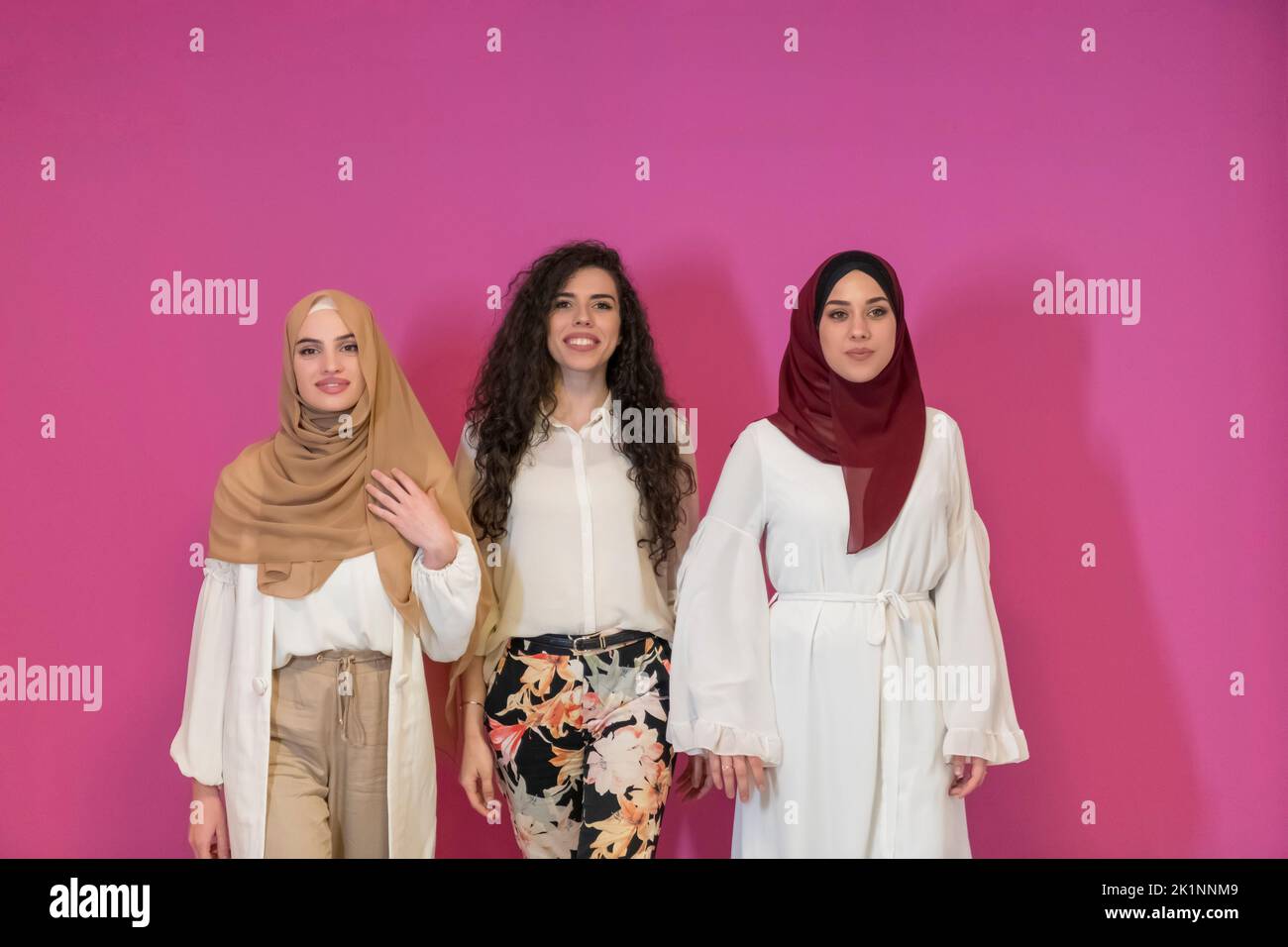 three Muslim women in hijab in a modern clothes pose against a pink ...
