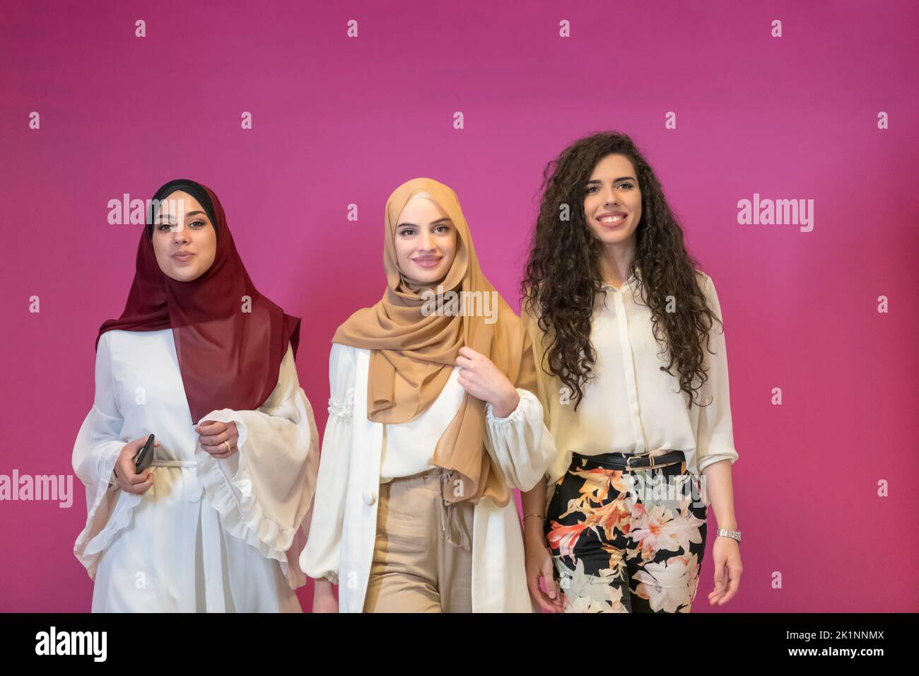 three Muslim women in hijab in a modern clothes pose against a pink ...