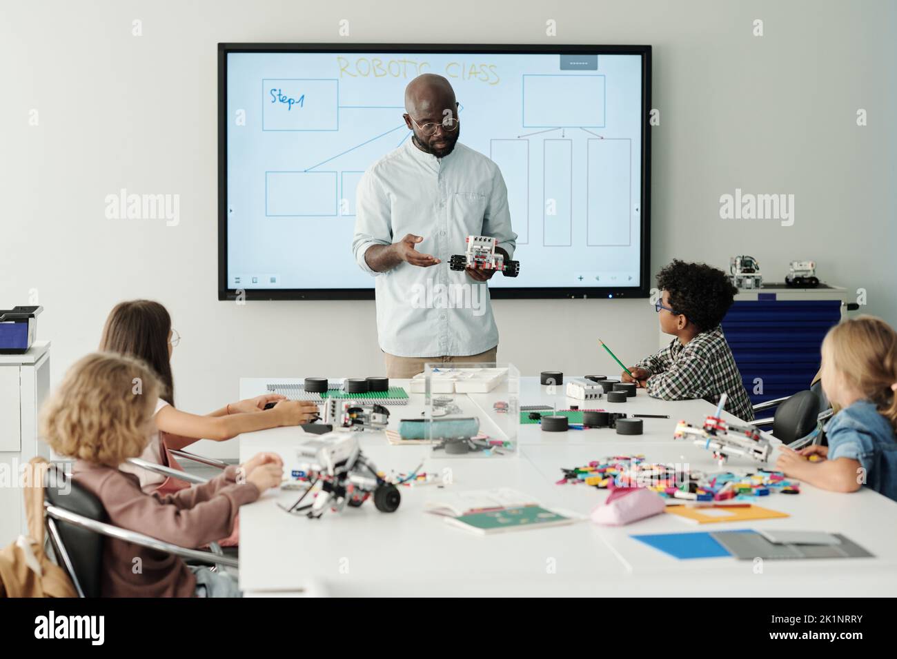Confident male teacher of robotics explaining intercultural elementary ...