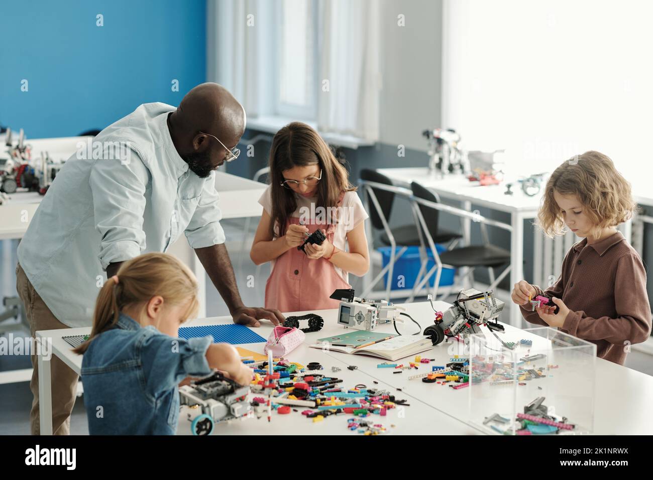 Group of youthful learners constructing new robots at lesson with ...