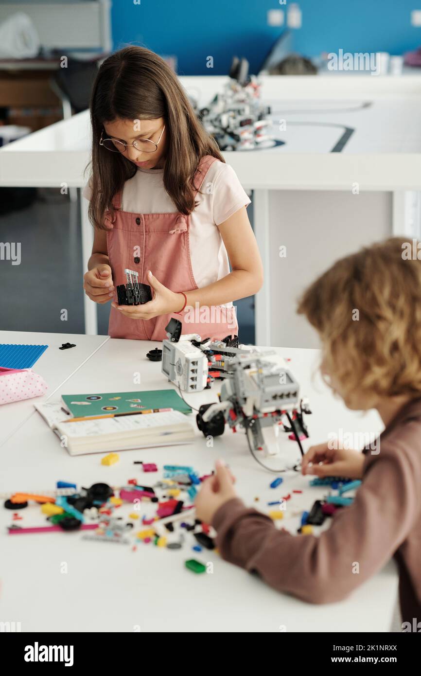 Two elementary schoolkids standing by table with details of robot at ...