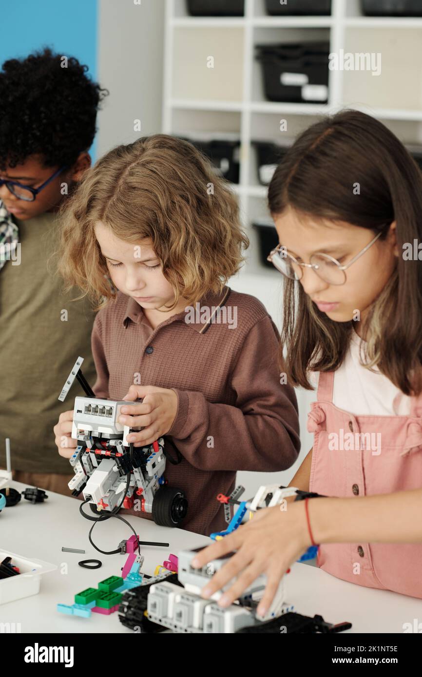 Group of youthful intercultural schoolchildren connecting details while ...
