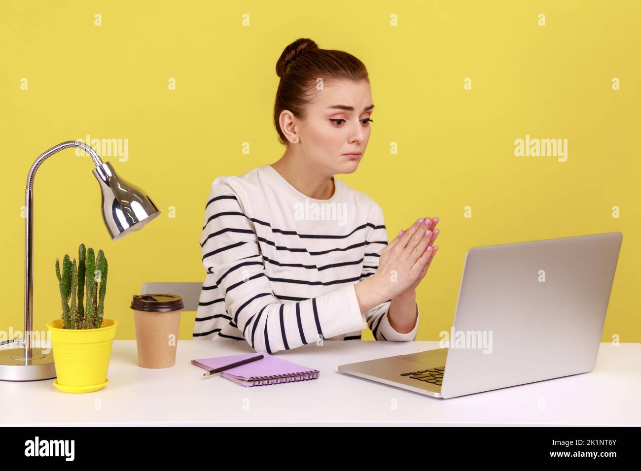 Woman in striped shirt holding hands in praying gesture and talking on ...