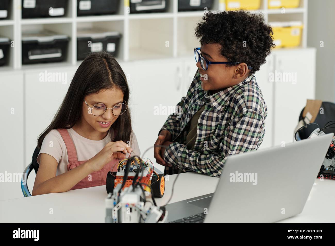 Two happy youthful learners of elementary school creating toy robot at ...