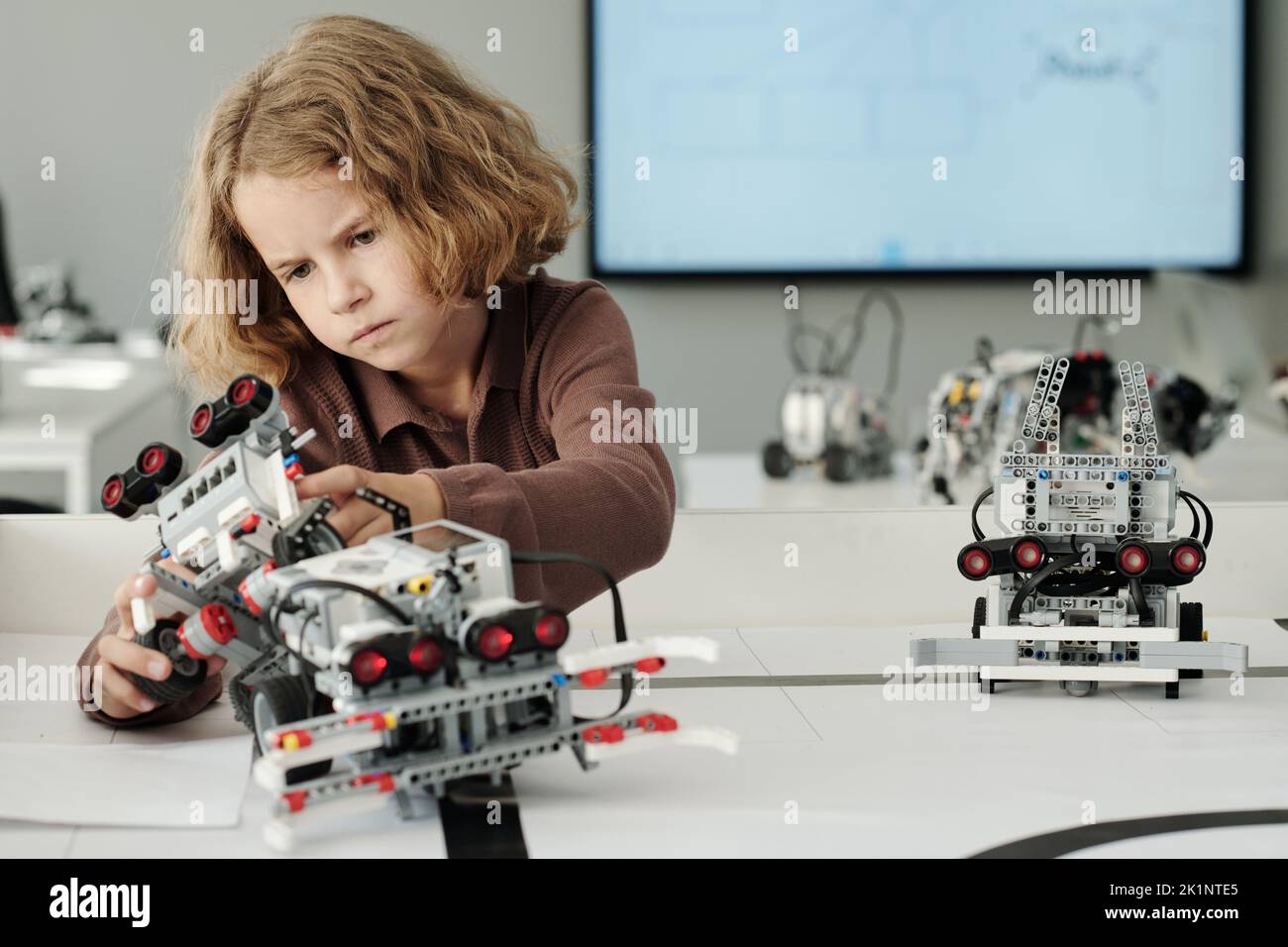 Clever youthful schoolboy sitting by desk at lesson of robotics and ...