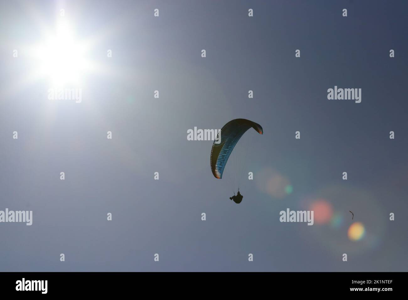 Paraglider in flight with gleaming sunshine silhouetting the glider ...
