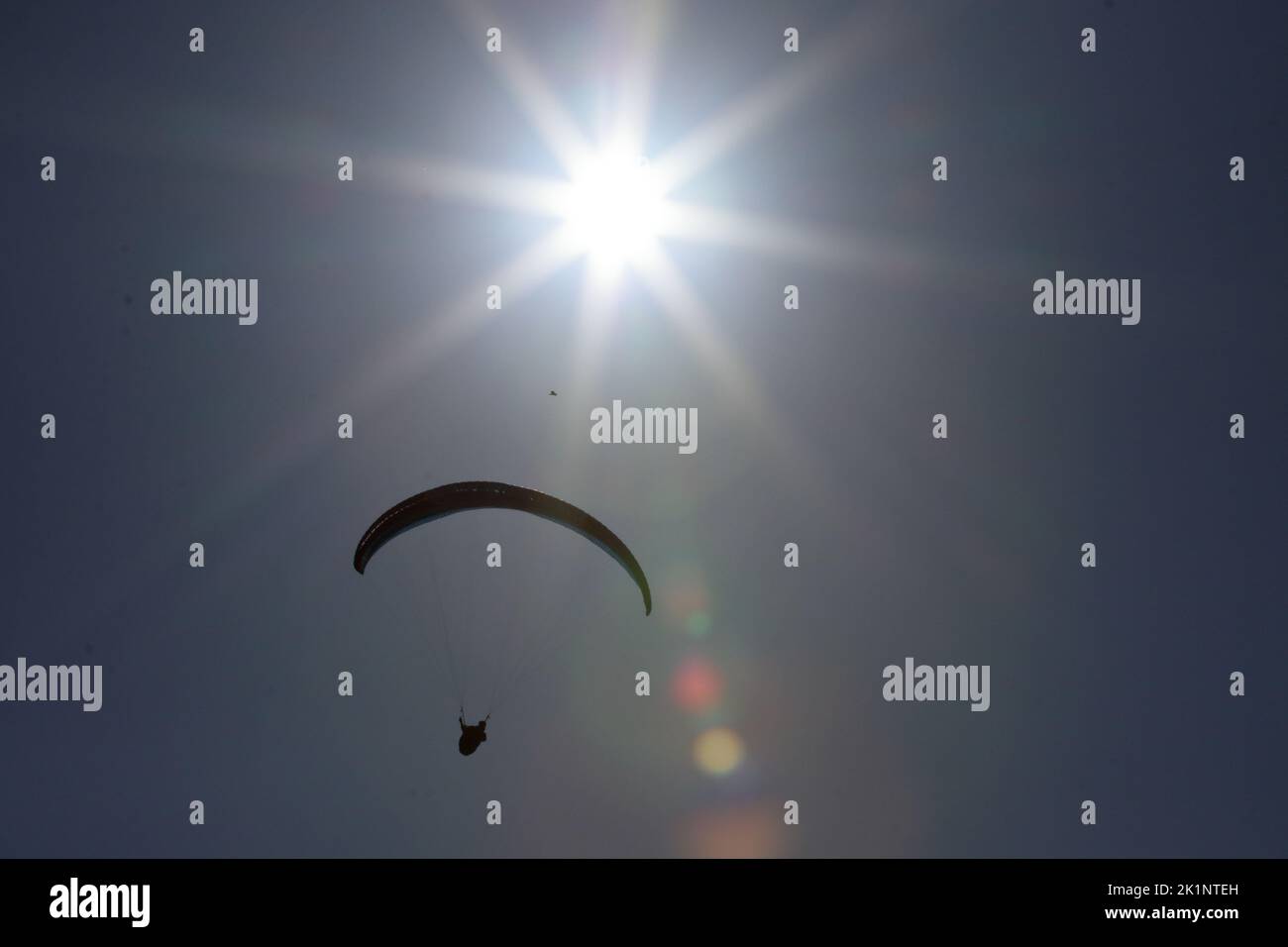 Paraglider in flight with gleaming sunshine silhouetting the glider ...