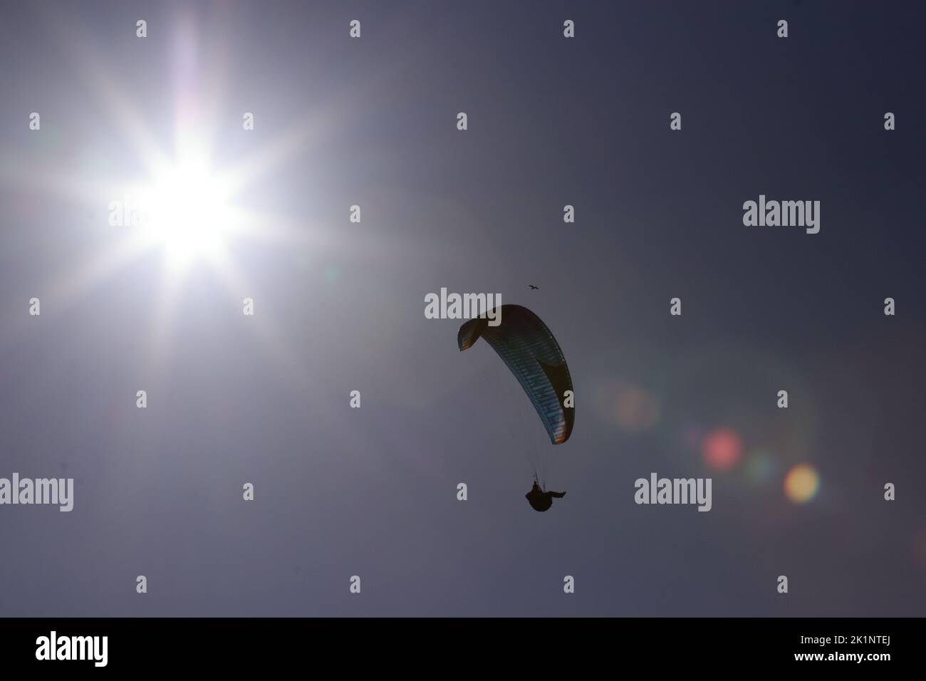 Paraglider in flight with gleaming sunshine silhouetting the glider ...