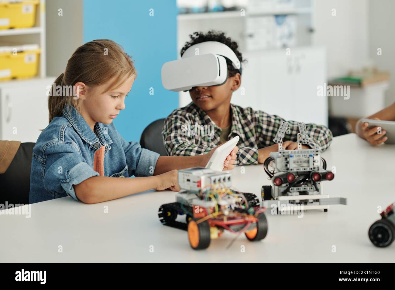 Cute schoolboy with vr headset turning head towards his classmate with ...