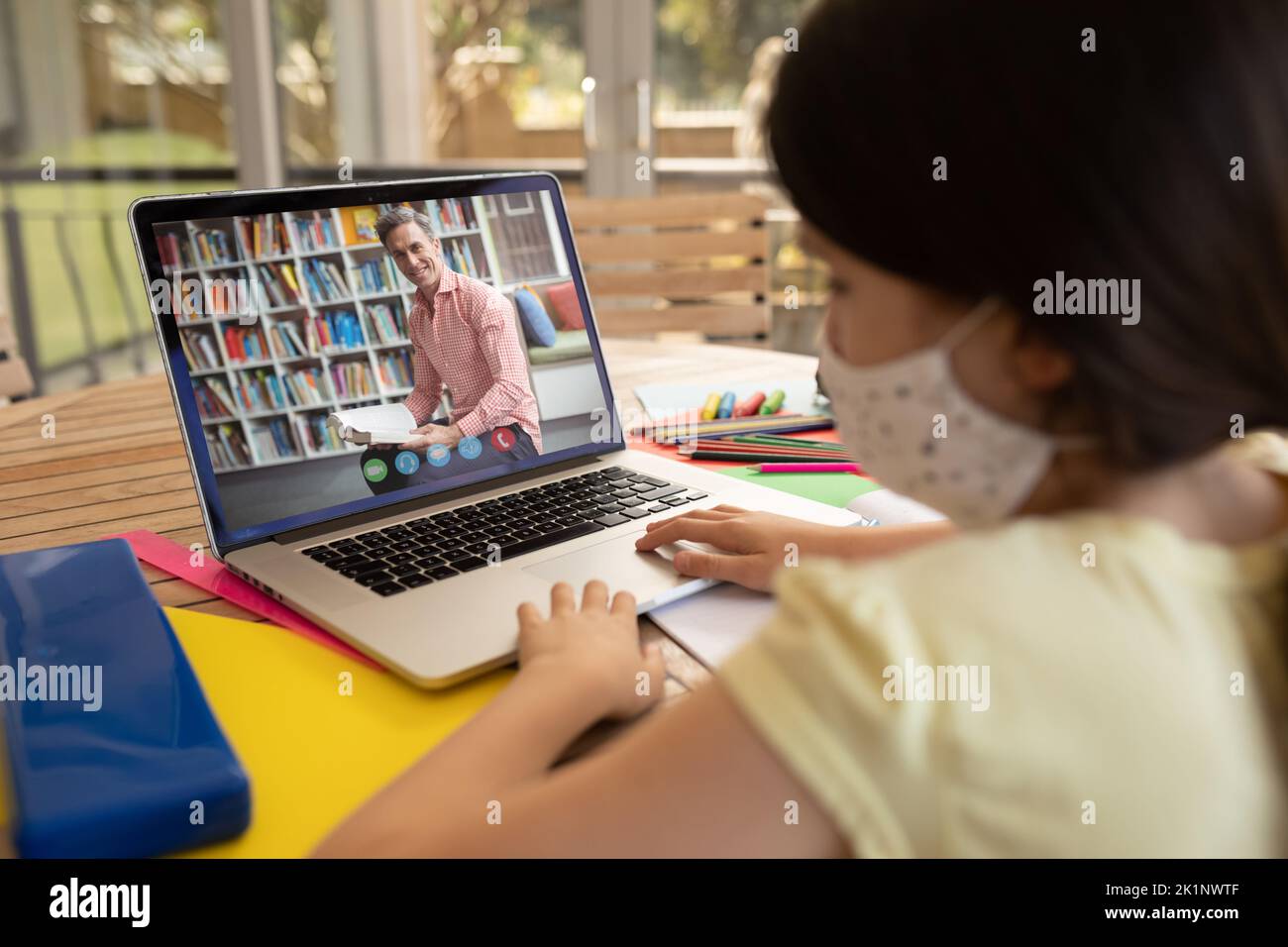 Female student wearing face mask having a videocall with male teacher ...
