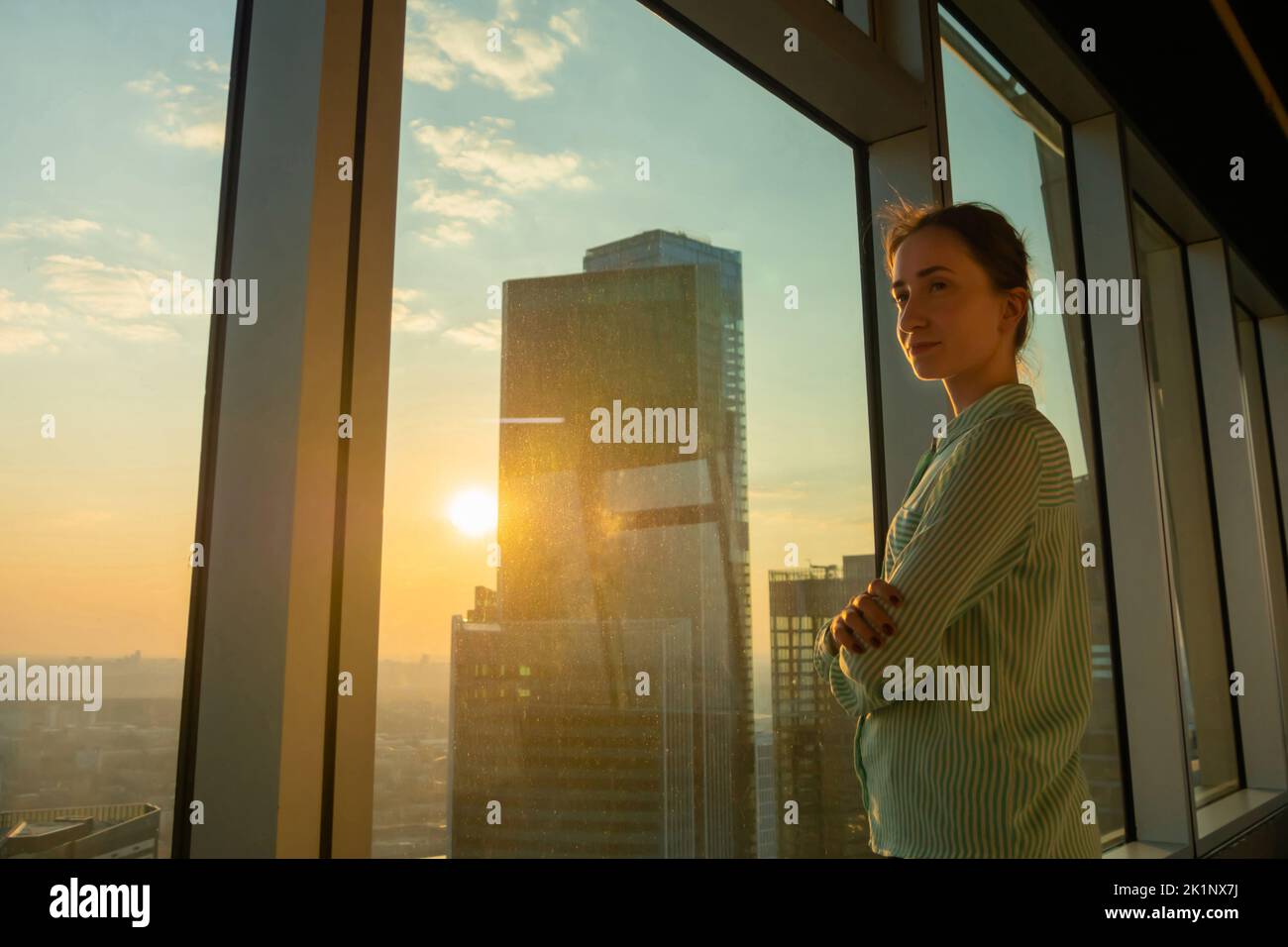 Portrait of woman looking at cityscape through window of skyscraper ...