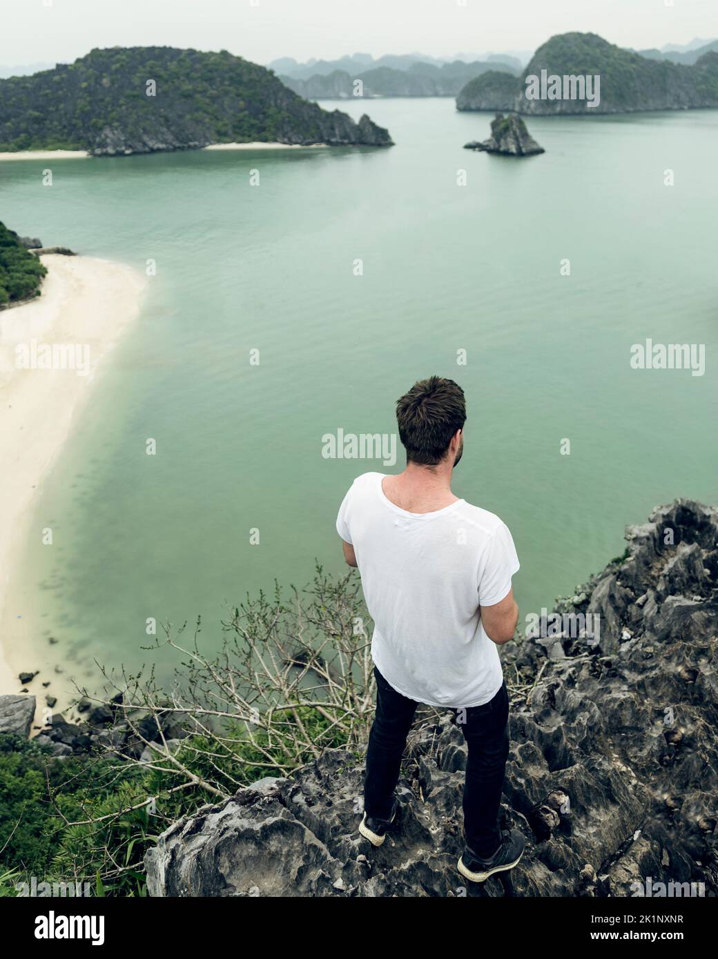 Man standing on the rocks contemplating the sea. Mountains can be seen ...