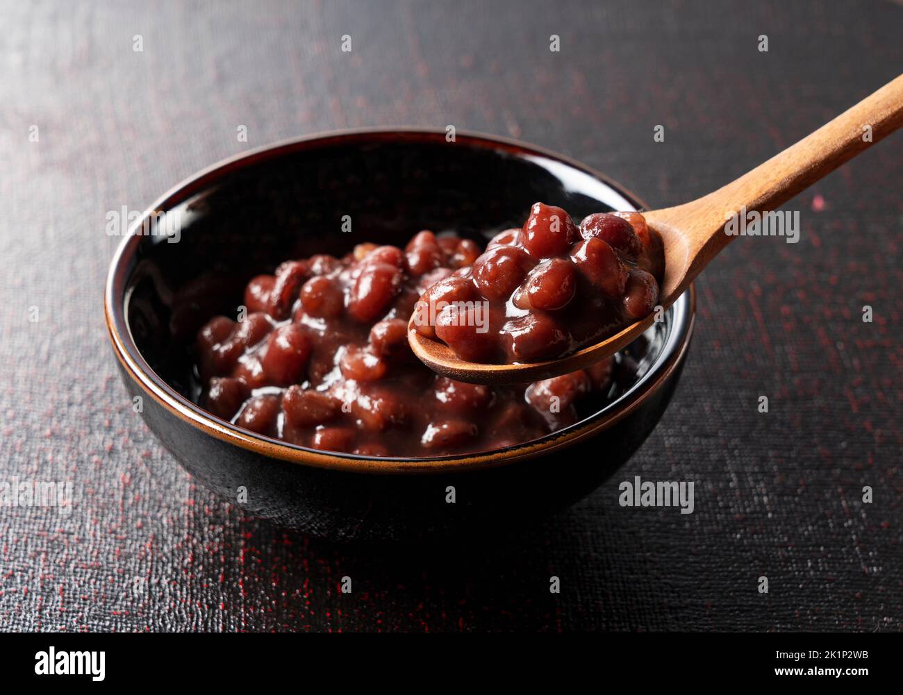 Boiled azuki beans in a small black bowl placed against a black ...