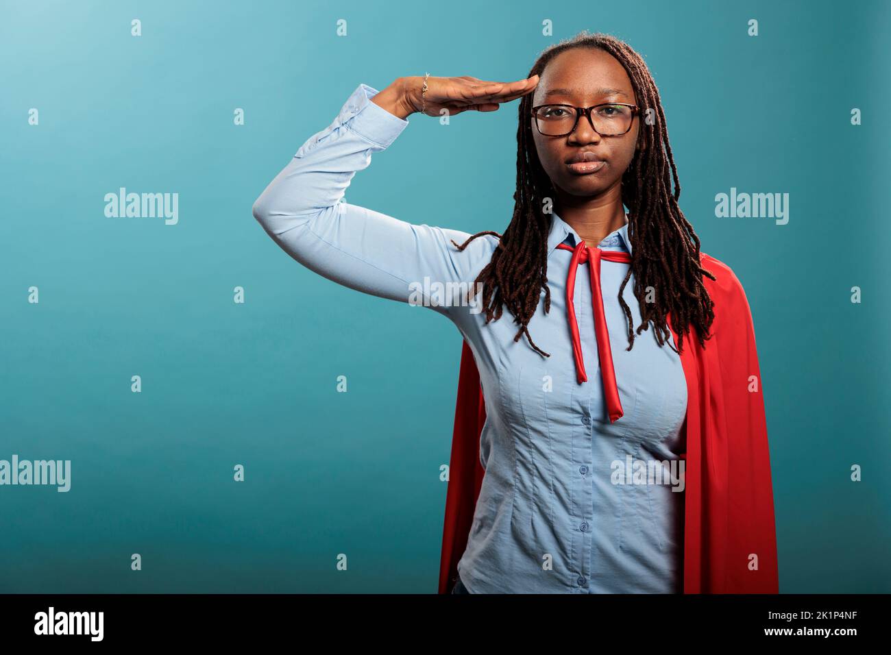 Serious and confident superhero woman standing on blue background while ...