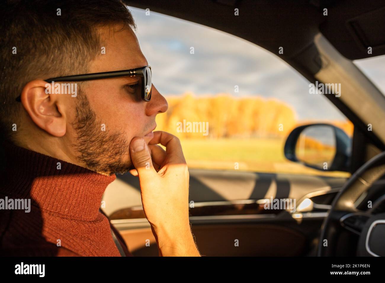 A man with a beard in a sweater rides in an expensive car. Front view ...