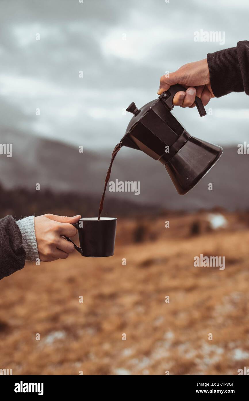 Person pouring out coffee from moka pot into cup outdoors with fog ...