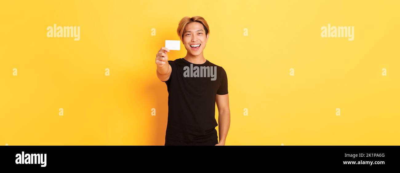 Cheerful handsome asian guy smiling pleased and showing credit card ...