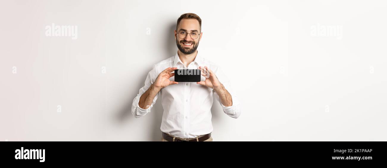 Handsome bearded man in glasses, demonstrating mobile phone application ...