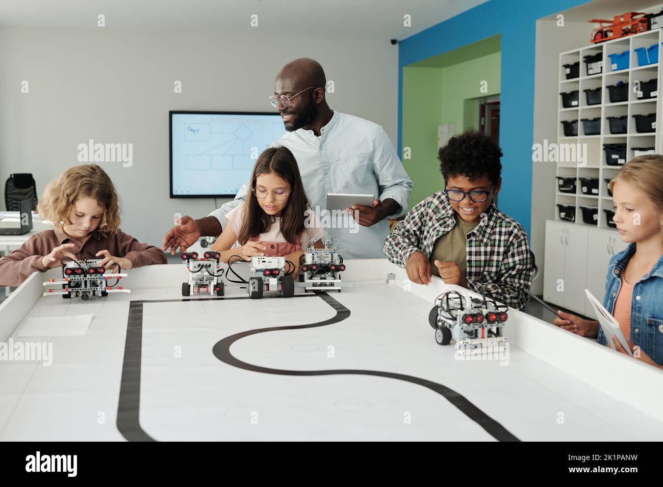 Young teacher of robotics with tablet helping schoolkids control their ...