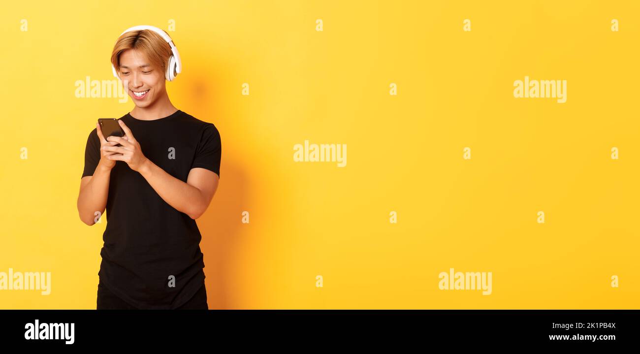 Young smiling asian guy using smartphone and listening music or podcast ...