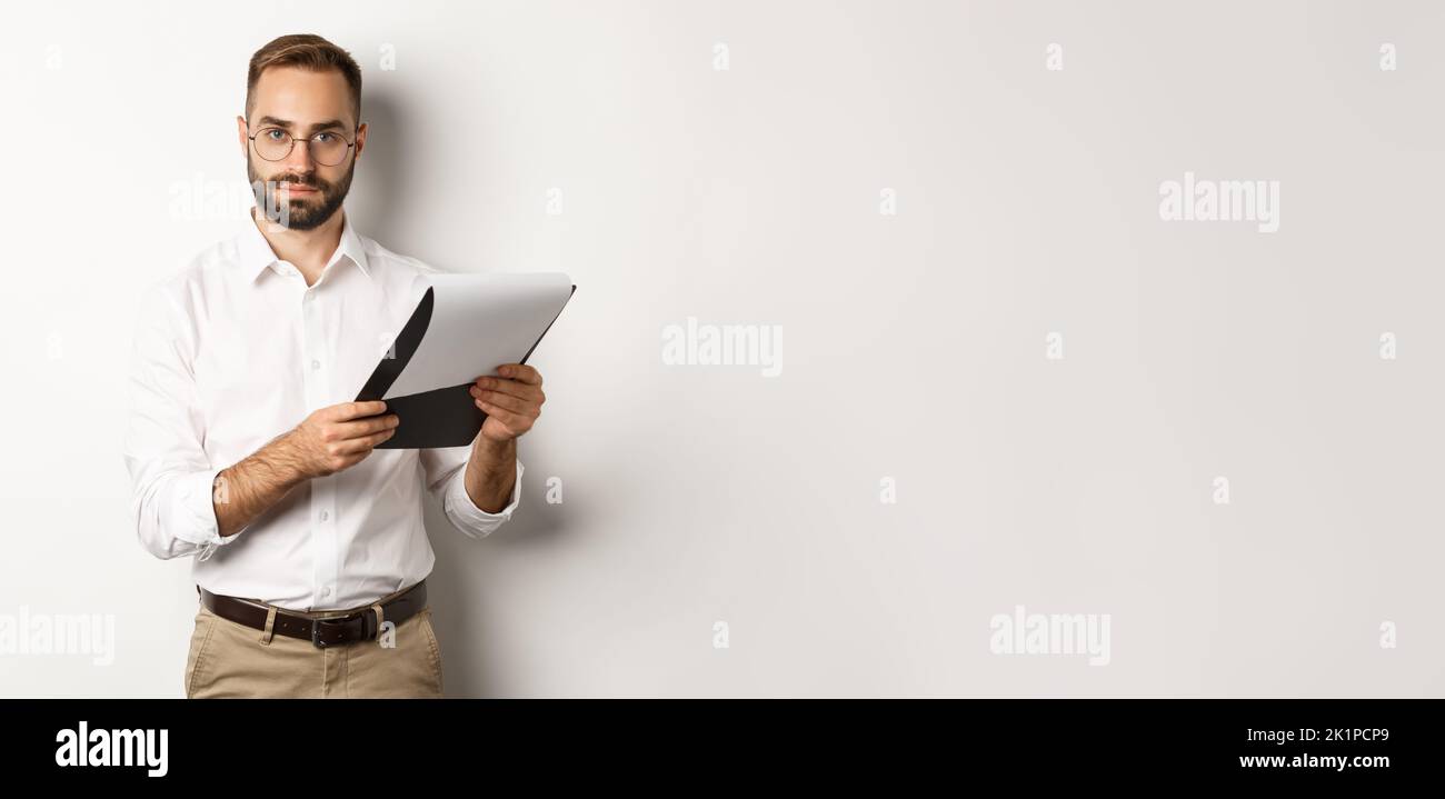 Serious employer looking at camera while reading documents on clipboard ...