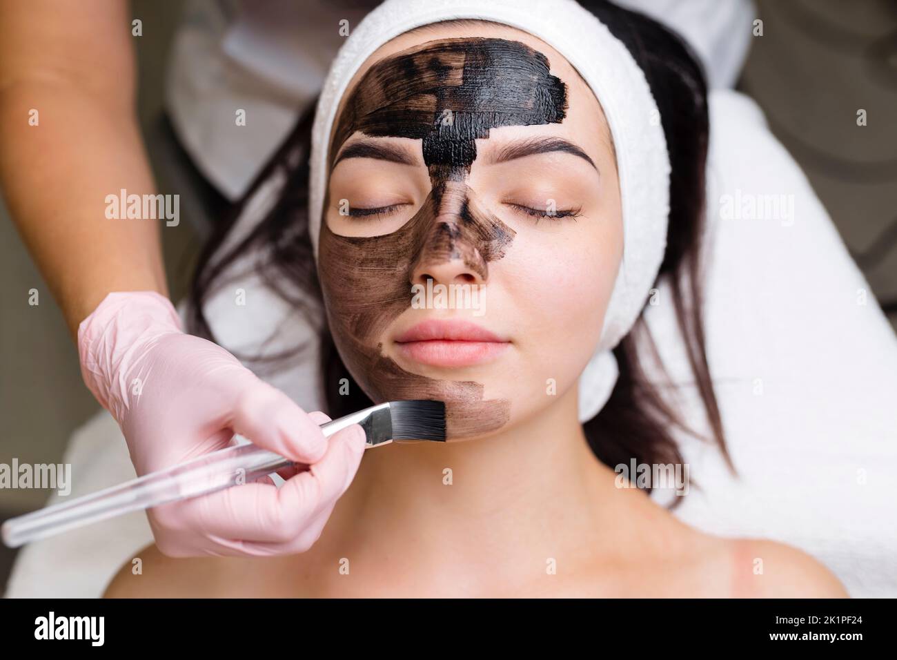 cosmetologist applying black mask on pretty woman face wearing black ...
