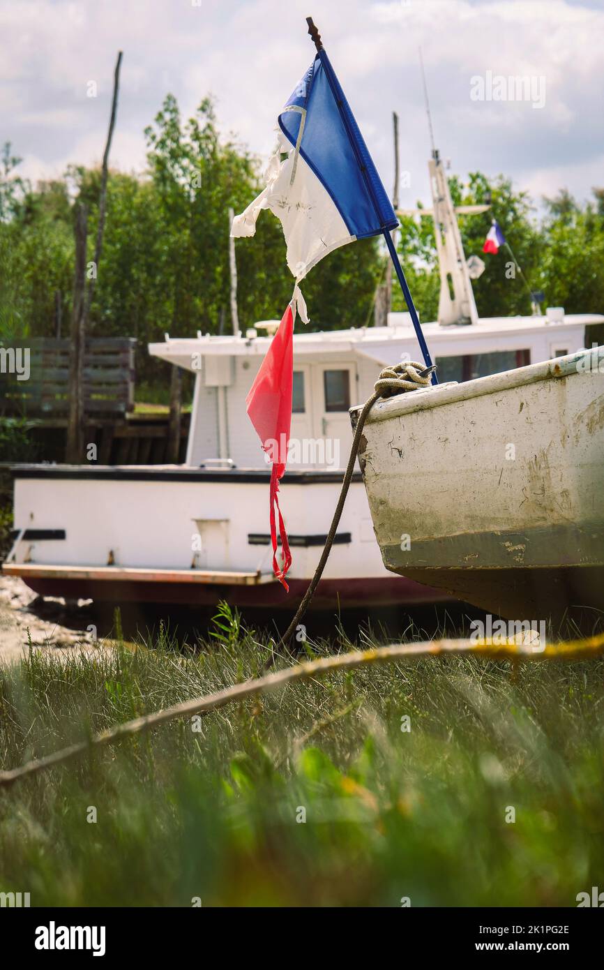 Ripped french flag on boats on dry land during low tide in small port ...