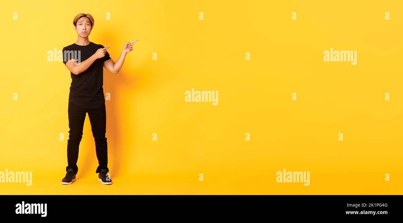 Full-length of sad and miserable asian guy in black clothes, pouting ...