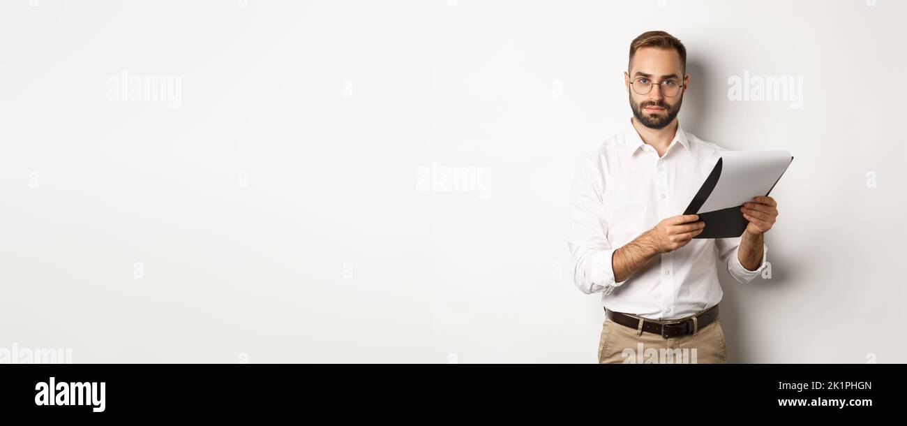Serious employer looking at camera while reading documents on clipboard ...