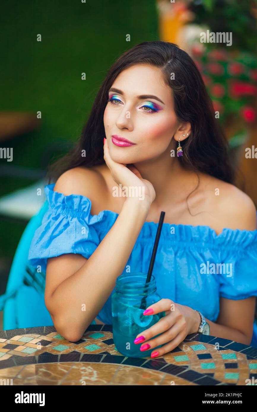 Young brunette woman with long hair in blue crop top is sitting at ...