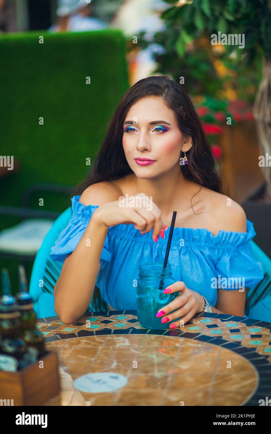 Young brunette woman with long hair in blue crop top is sitting at ...