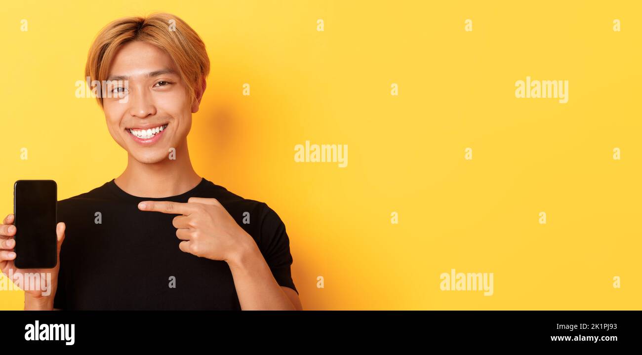 Cheerful attractive korean guy pointing finger at mobile phone screen ...