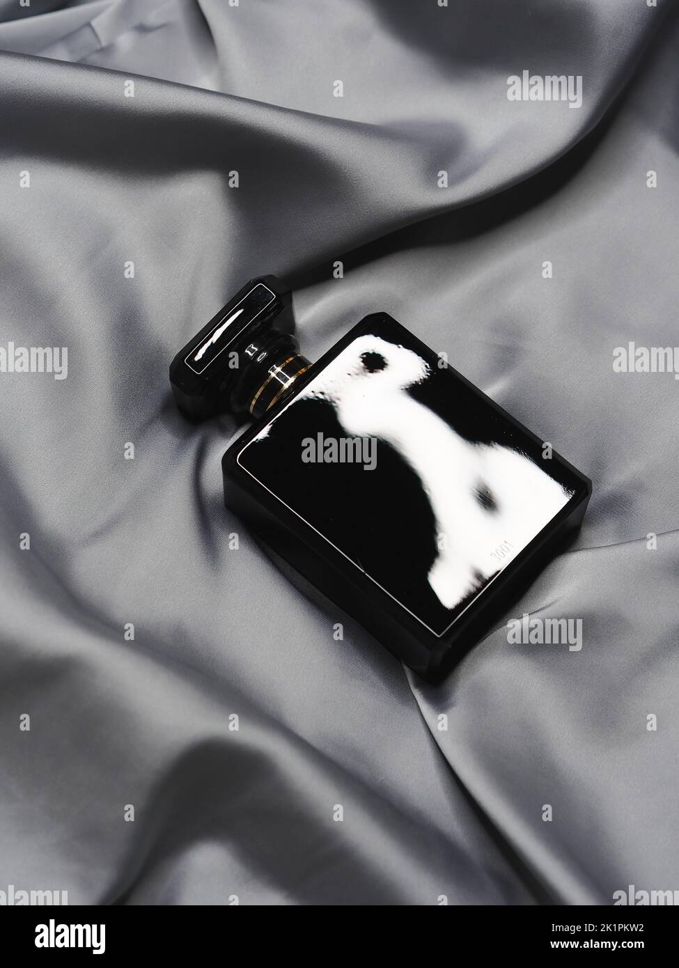 A vertical closeup high-angle of a black perfume bottle on a grey silk ...