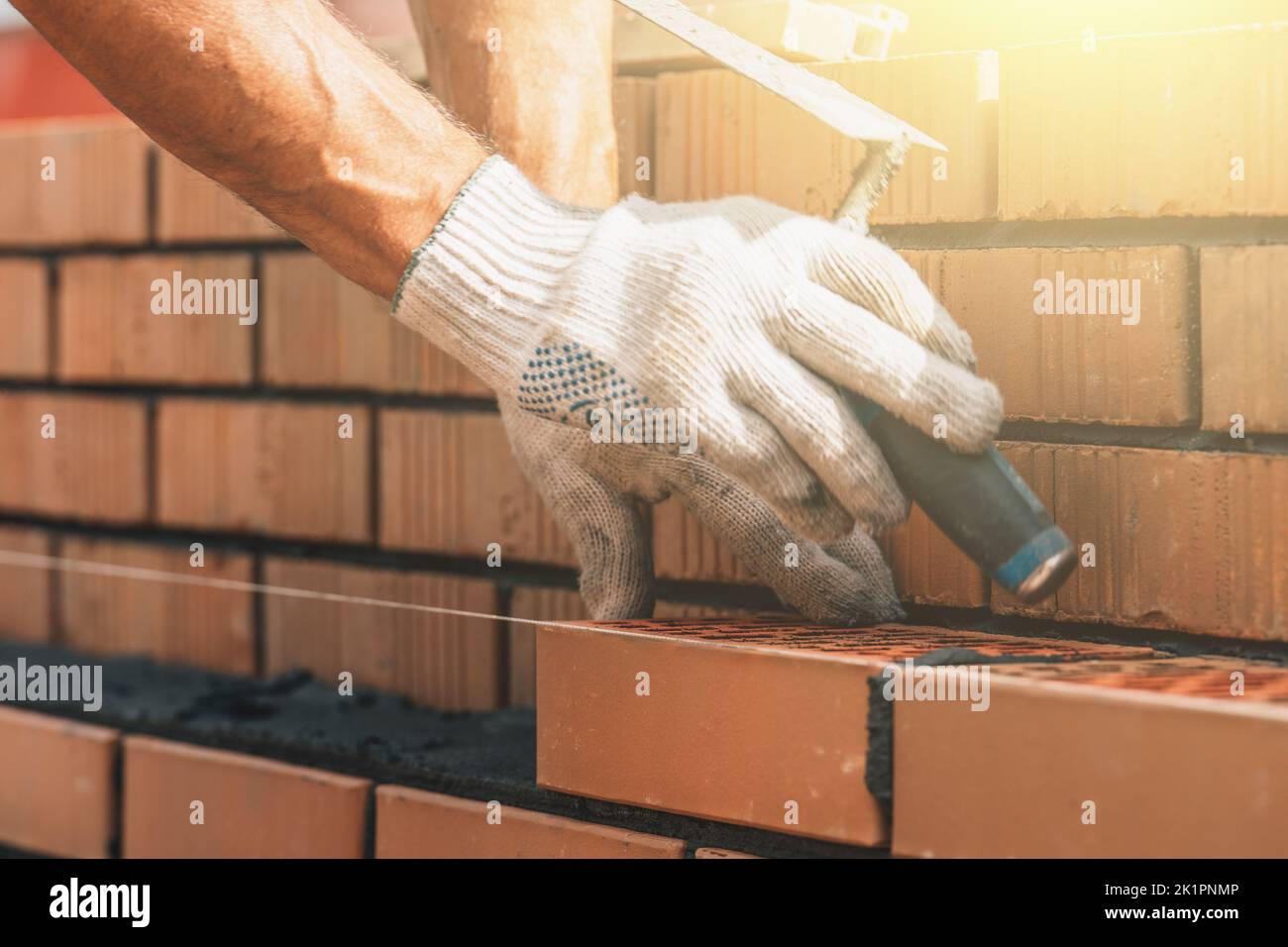 Bricklayer taps with trowel on newly laid brick on cement mortar. Brick ...
