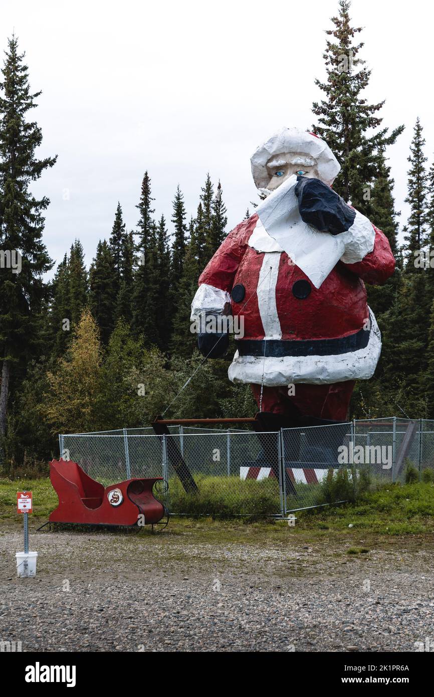 A vertical shot of a Santa Claus statue against green trees in a park ...