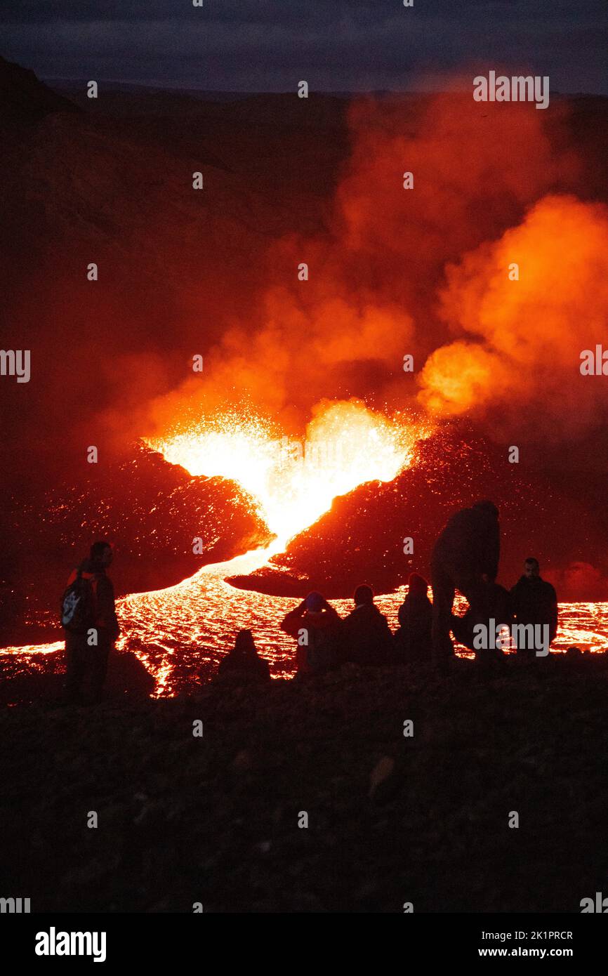 A vertical shot of a group of people watching lava flowing from a ...