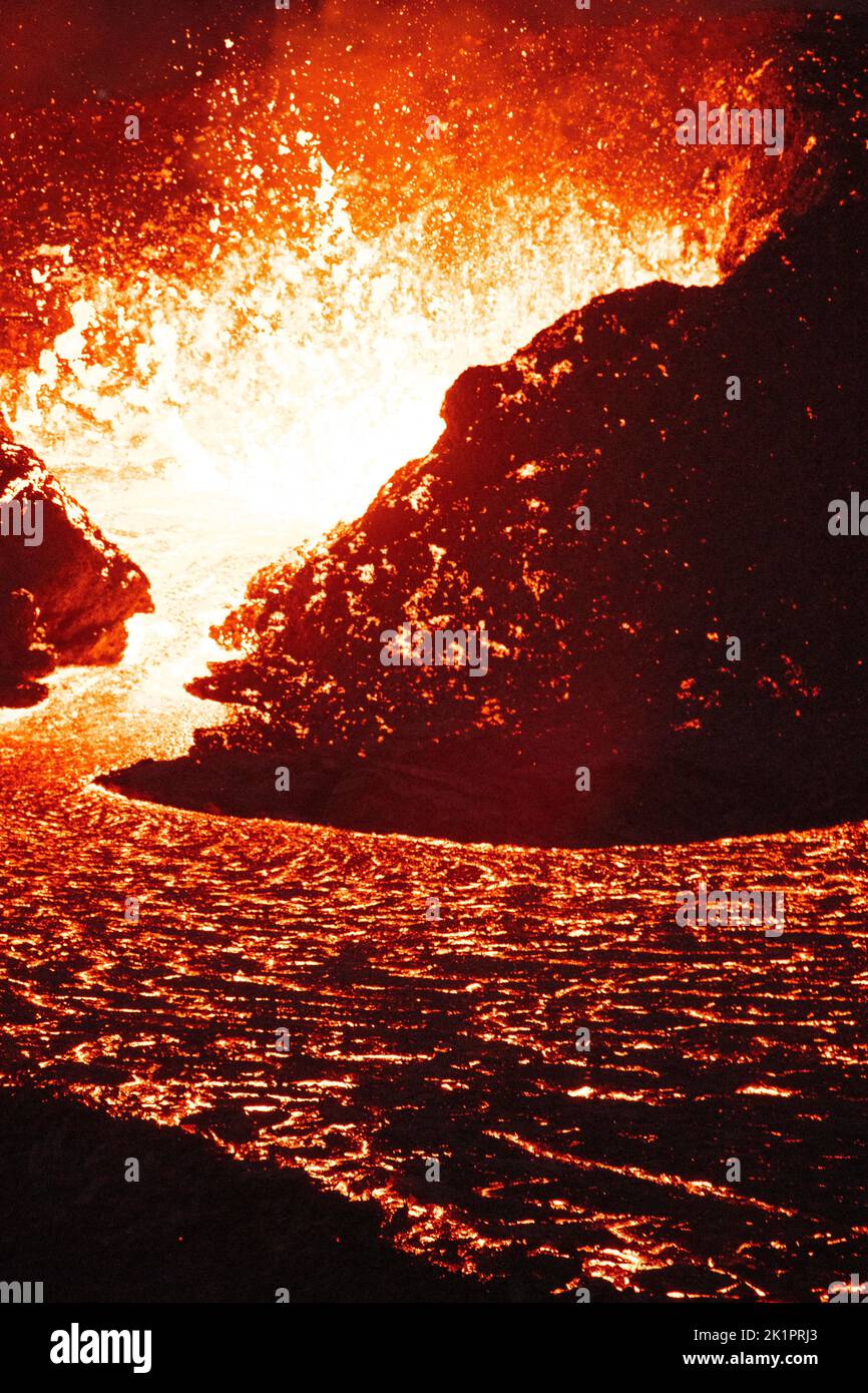 A vertical shot of lava splashing from a volcano at night in Iceland ...