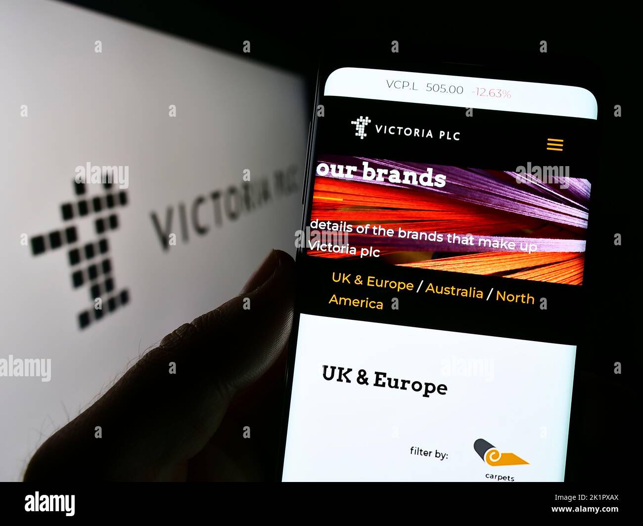 Person holding cellphone with webpage of British flooring company Victoria plc on screen in ...