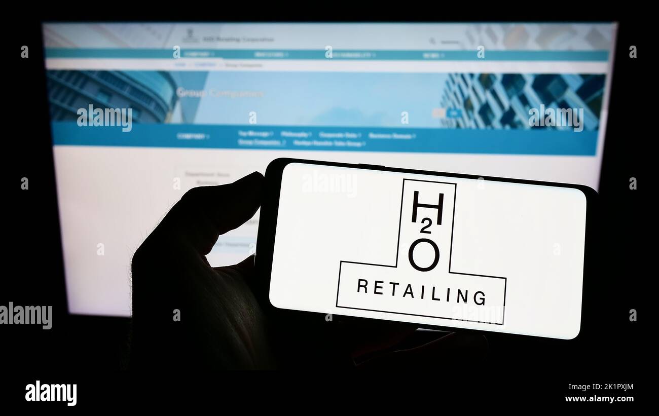 Person holding mobile phone with logo of Japanese company H2O Retailing ...