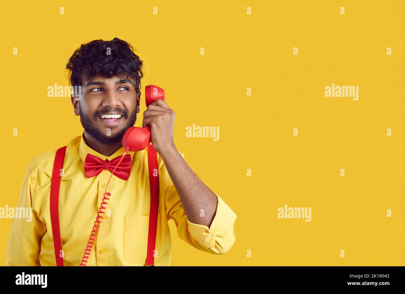 Cheerful funny indian man talking on landline retro telephone on orange ...