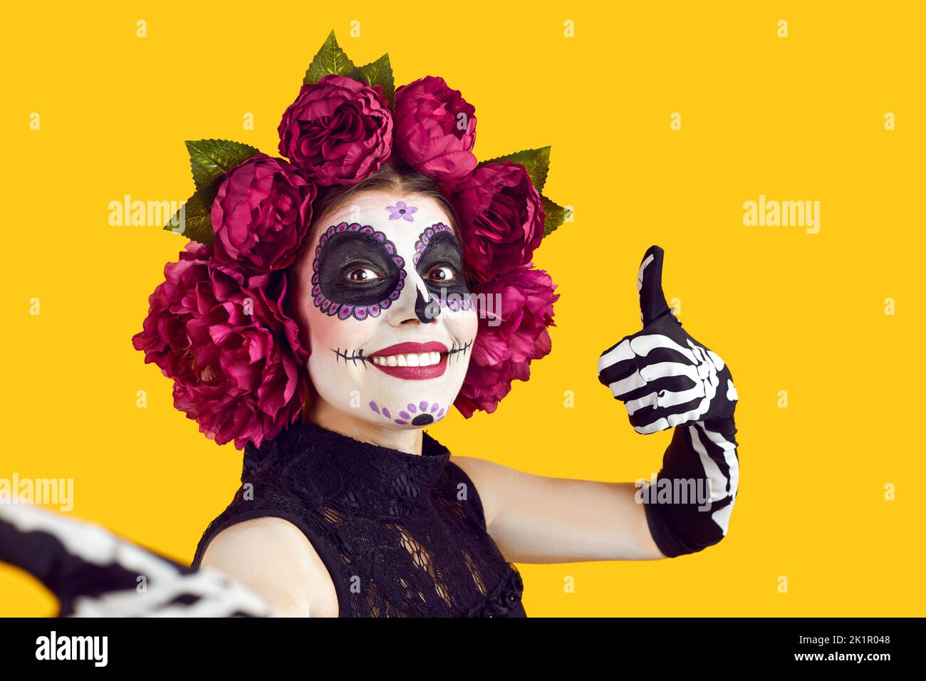 Crazy woman in Halloween costume with wreath of pink flowers and scary make-up shows thumb up ...