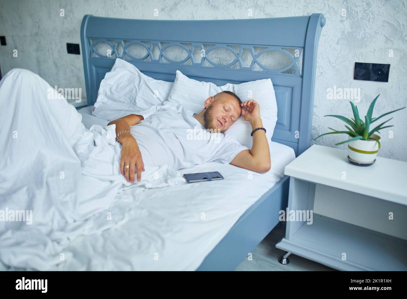 Bearded man sleeping alone on a big and cozy bed white linens with ...